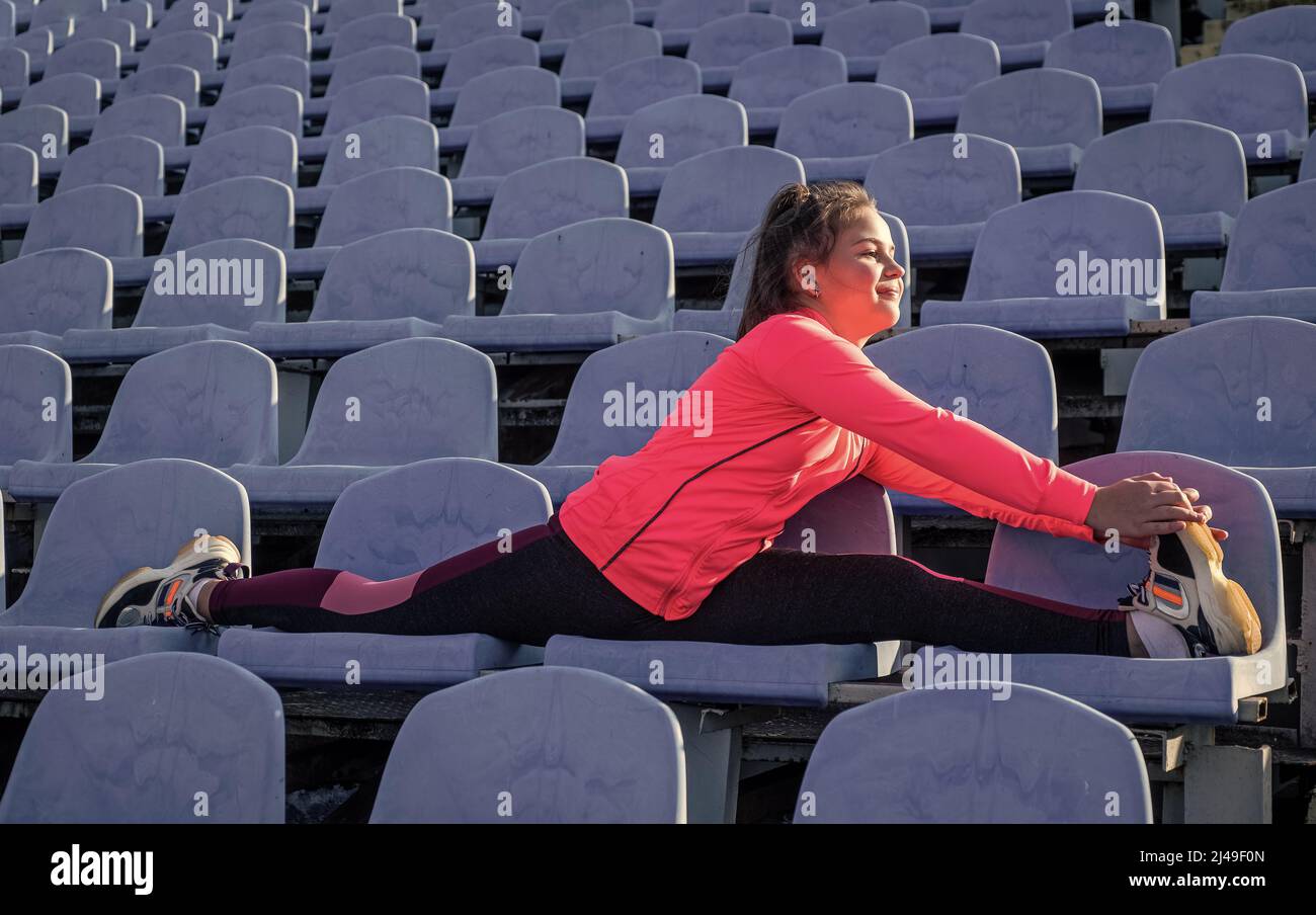 Flexible girl child in sportswear do splits stretching legs on stadium ...