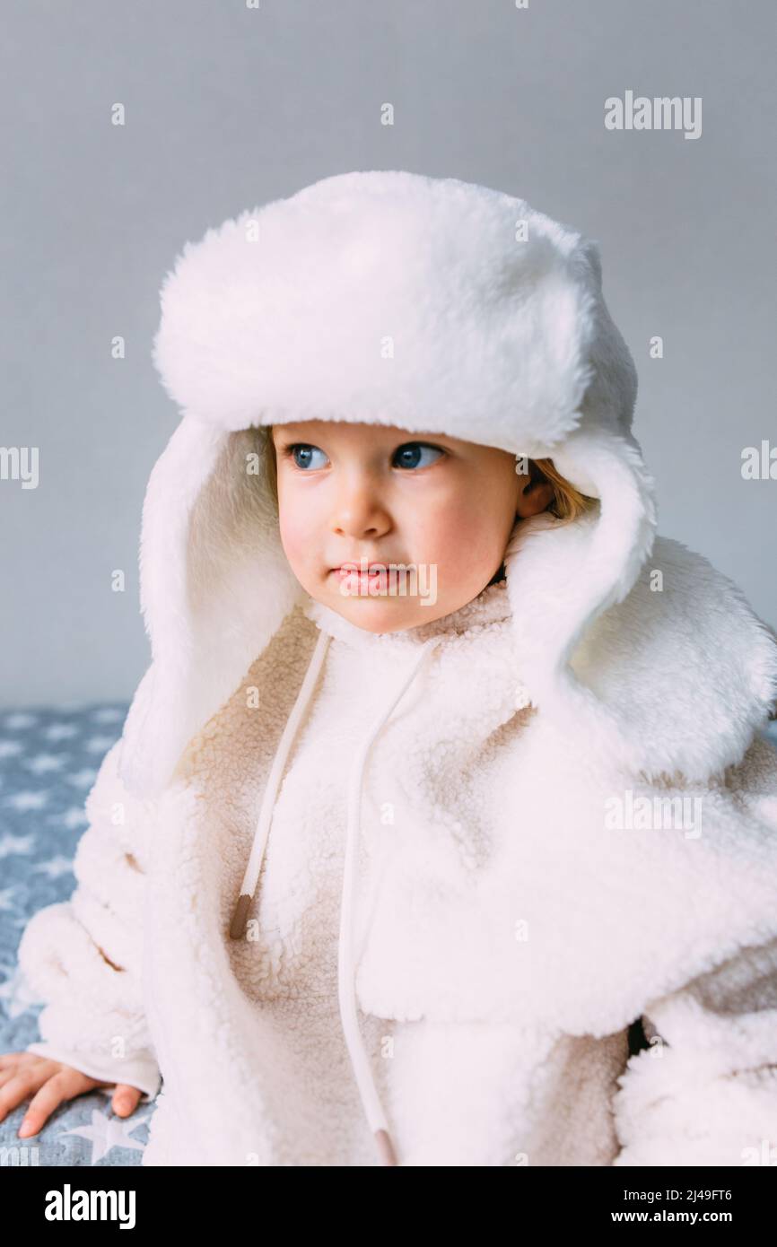 Cute child y on the bed in cozy adult clothes and a hat with earflaps ...