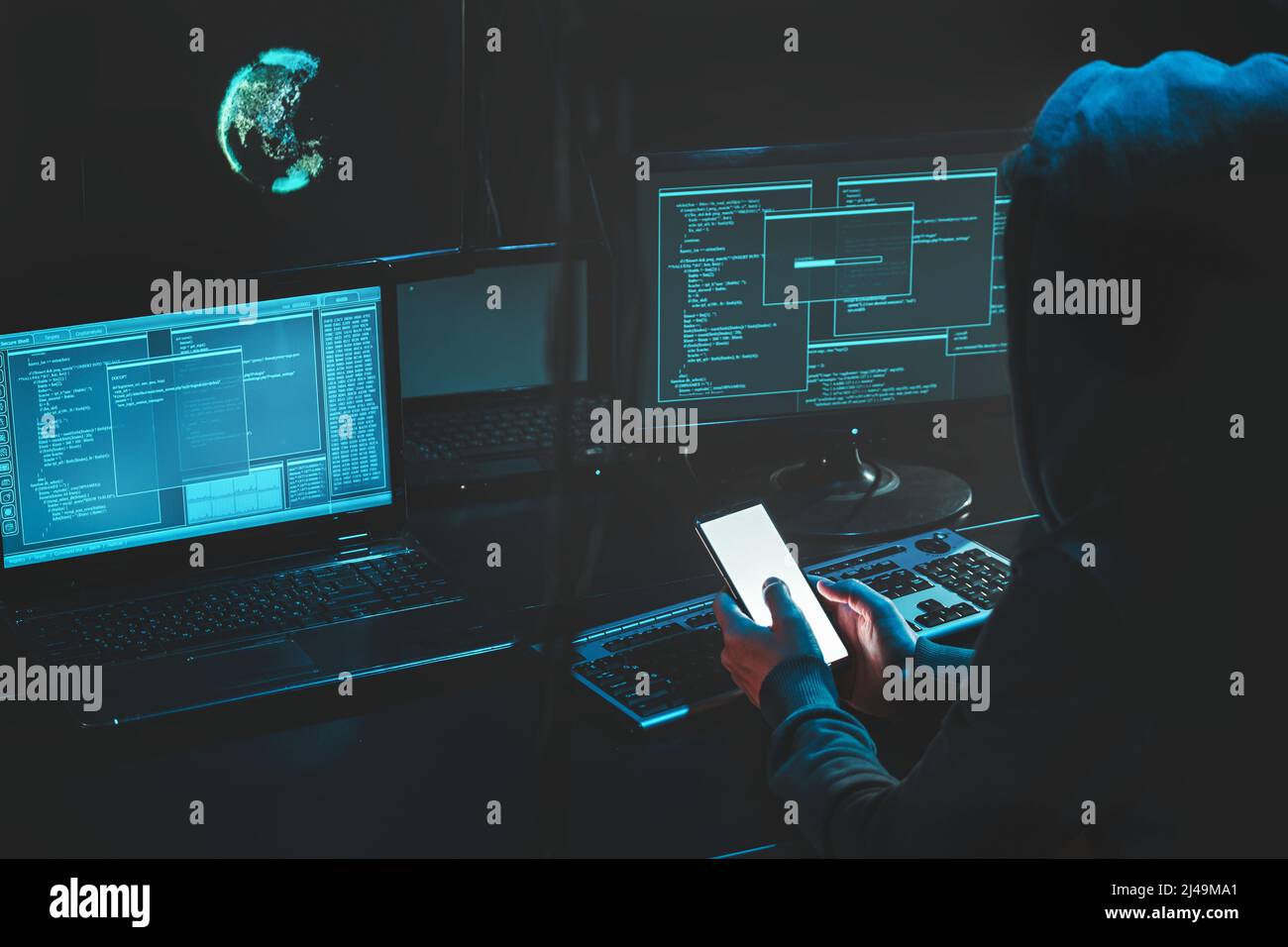 Overhead hacker in hood working at laptop and mobile phone typing text ...
