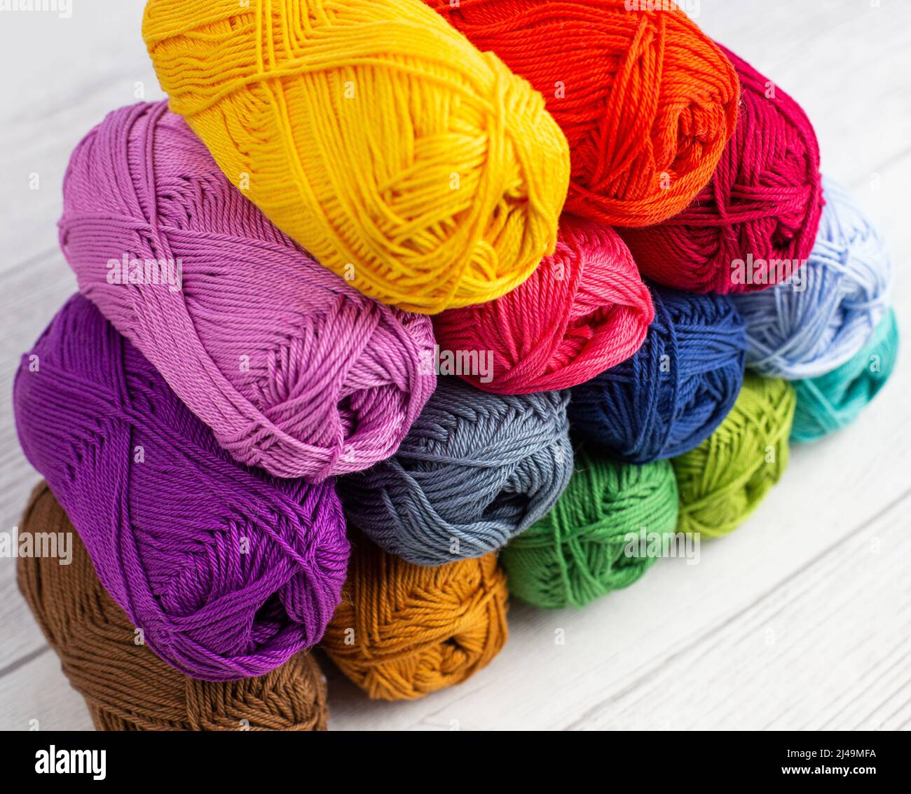 Rainbow colored skeins of yarn stacked in a pyramid on a light ...