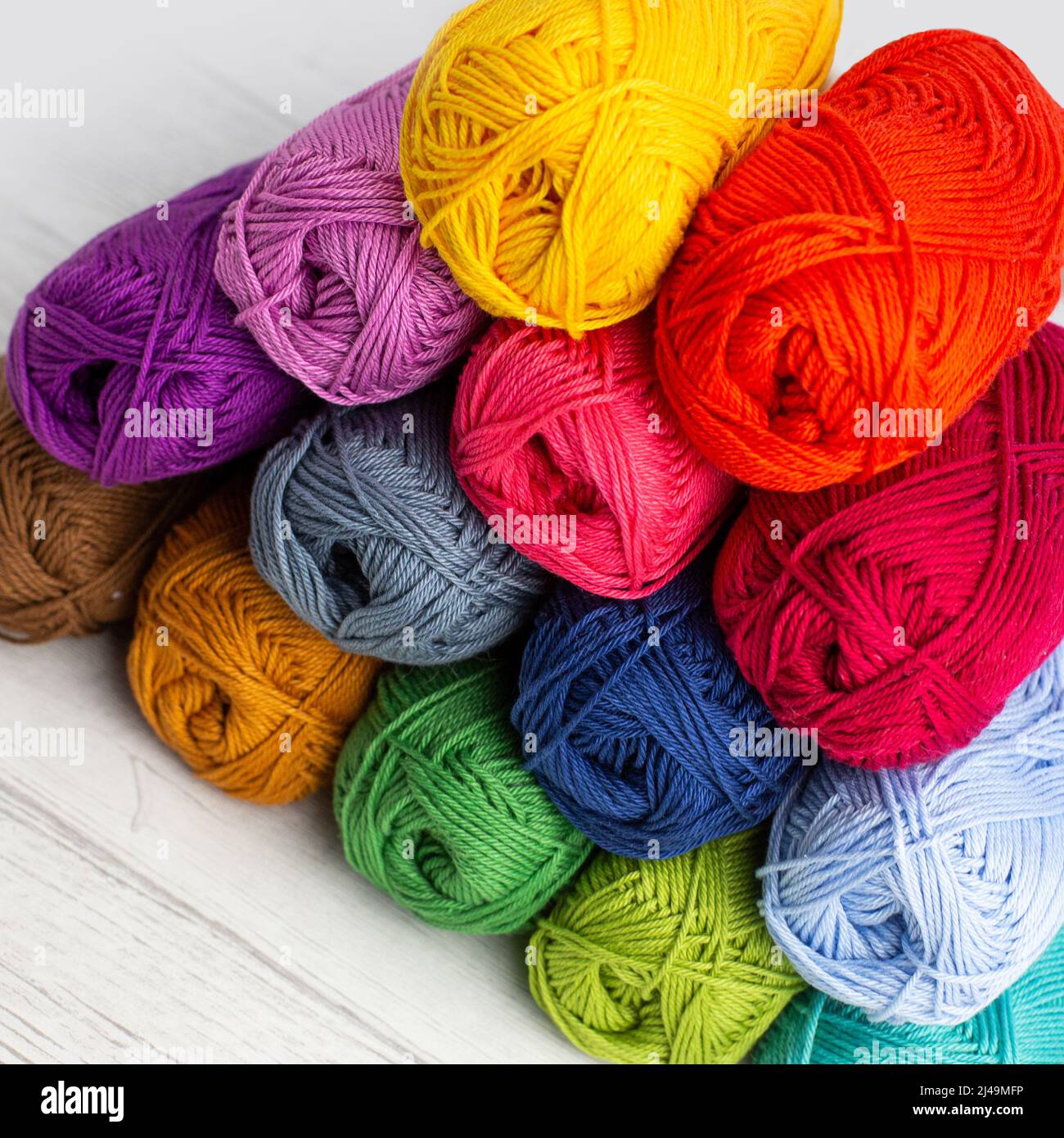 Rainbow colored skeins of yarn stacked in a pyramid on a light ...