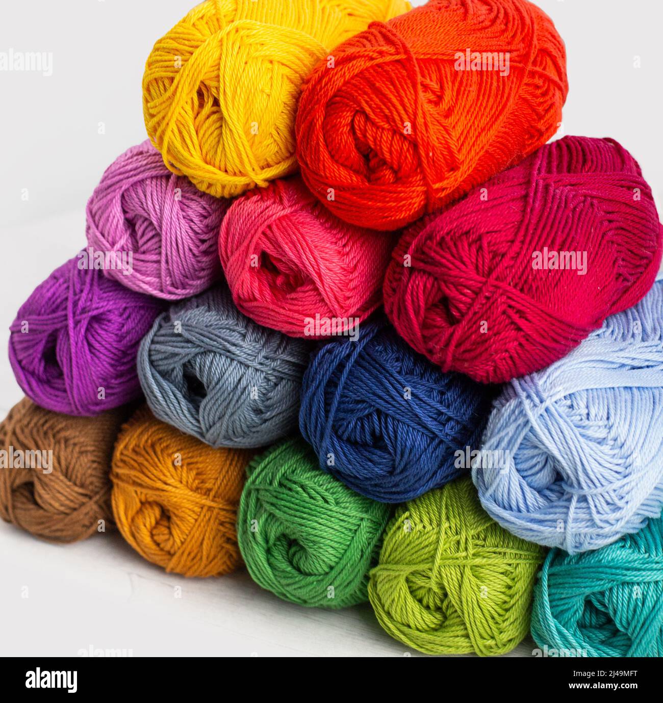 Rainbow colored skeins of yarn stacked in a pyramid on a light ...