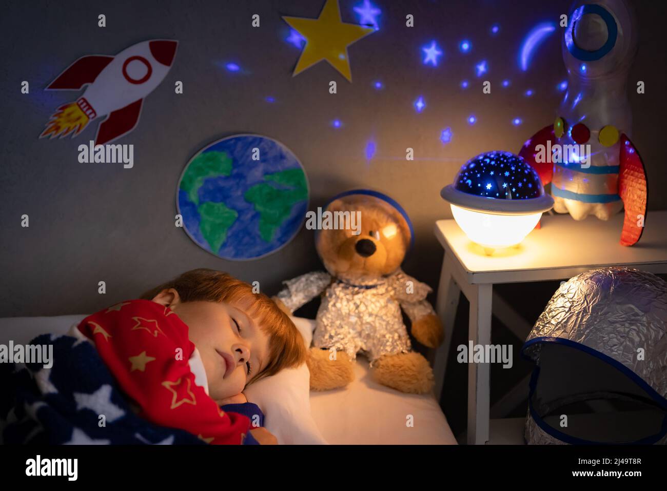 Happy child sleeping with toy rocket and teddy bear. Kid pretend to be ...