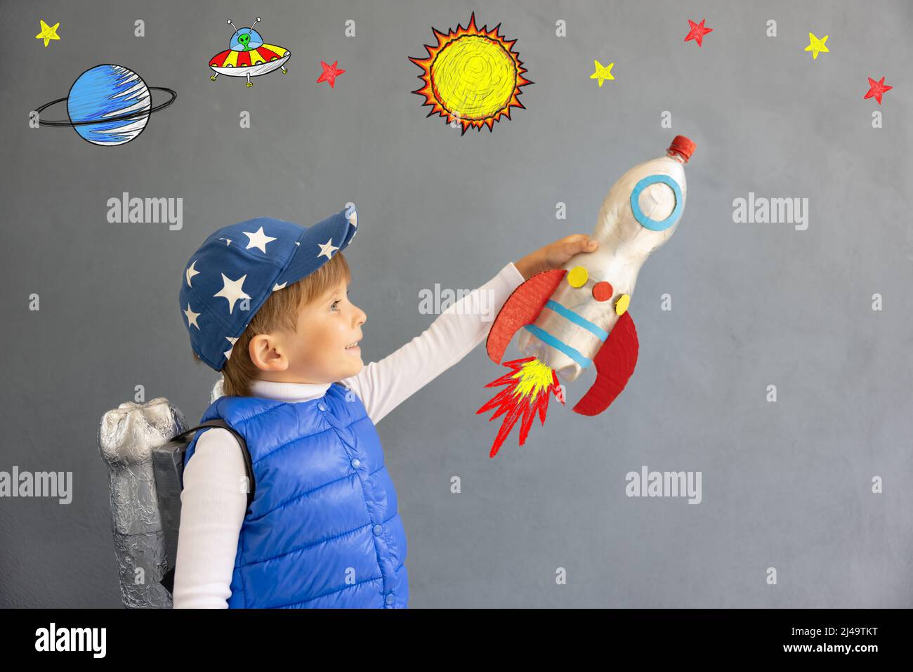 Happy child playing with toy rocket against concrete wall background ...