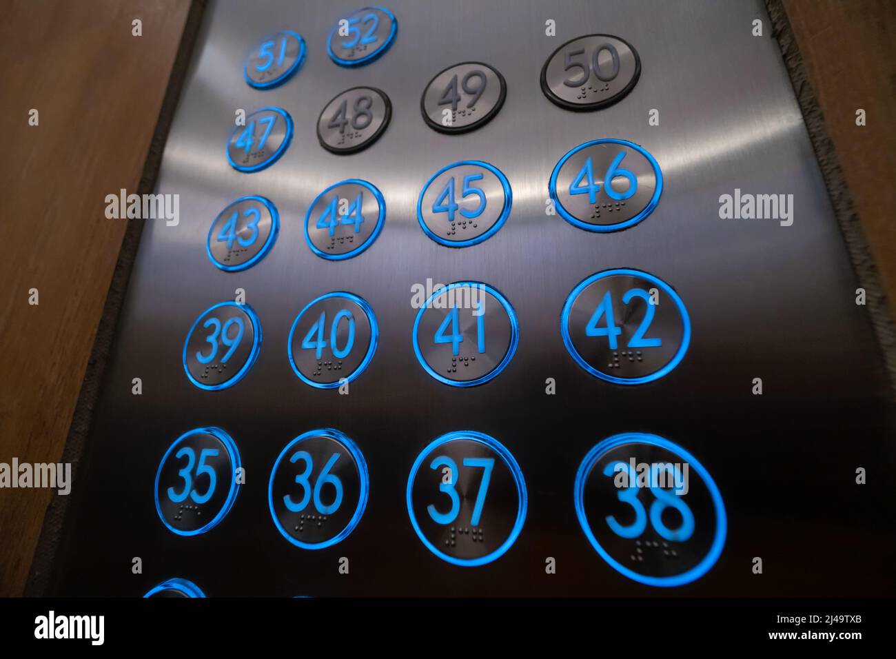 Close-up of blue glowing elevator buttons with Braille characters ...