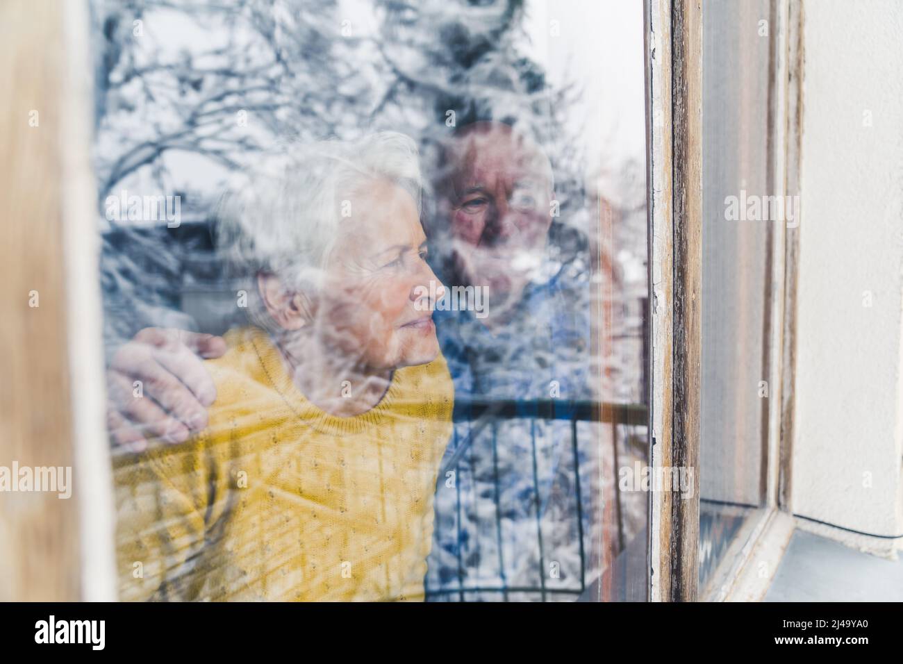View from behind the window glass. Two caucasian retired grandparents ...