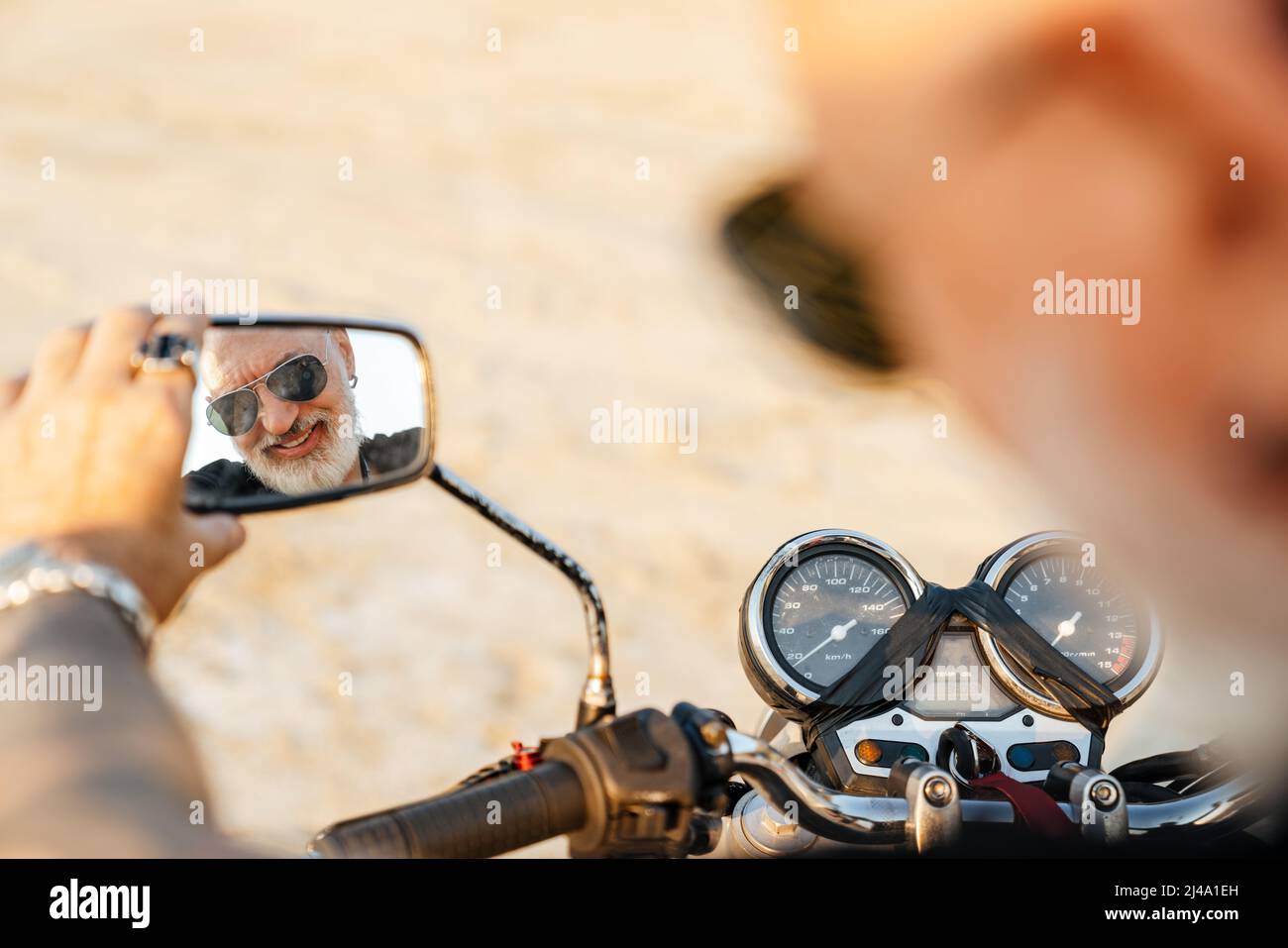 Bold senior man looking at rear-view mirror while riding motorcycle on ...
