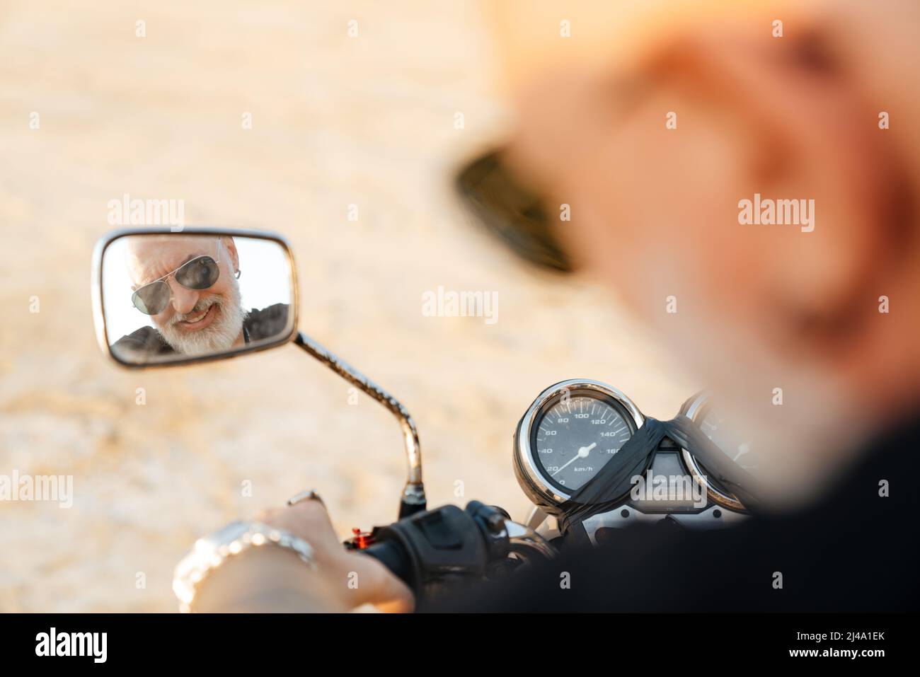 Bold senior man looking at rear-view mirror while riding motorcycle on ...