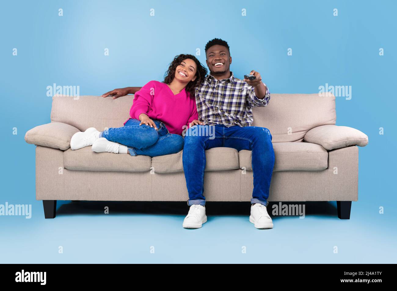 Excited young black couple with remote control sitting on couch and ...