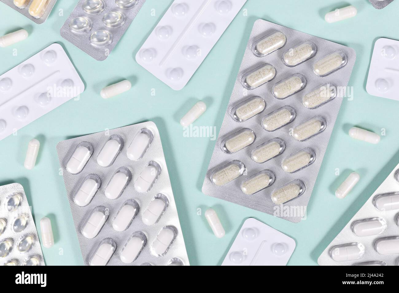 Various blister packs with pills and capsules on mint green background ...