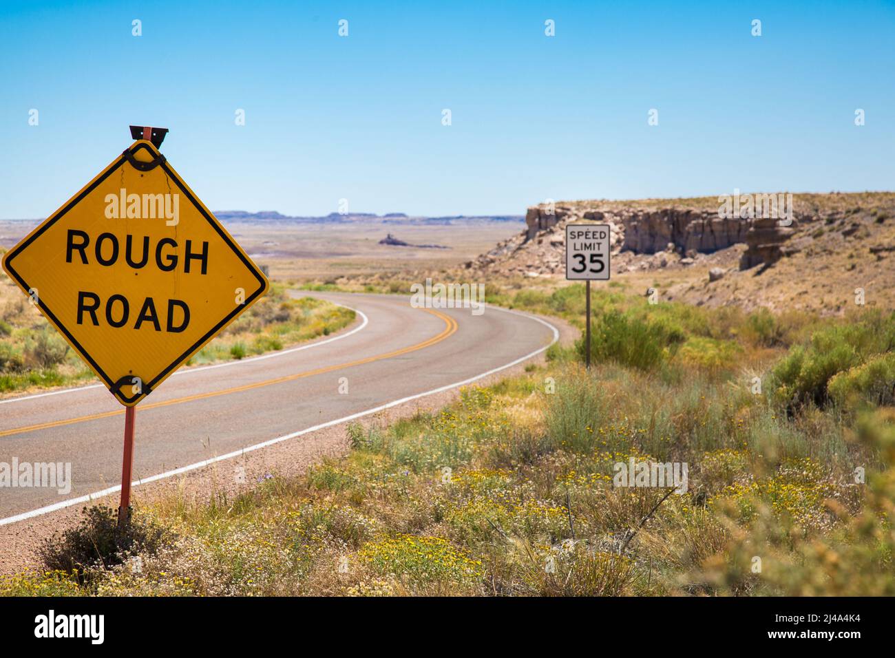 A 'rough road' sign on a bending stretch of desert highway in the ...