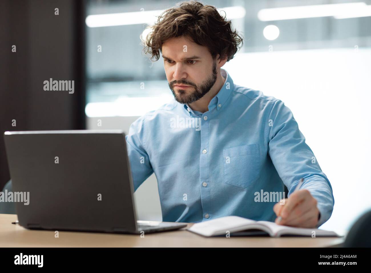 Portrait of focused man using laptop and writing in notebook Stock ...