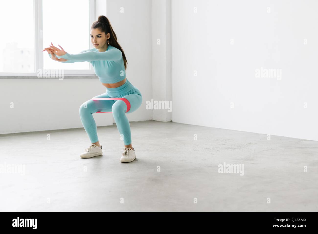 Slim woman works out with resistance band on white wall background ...