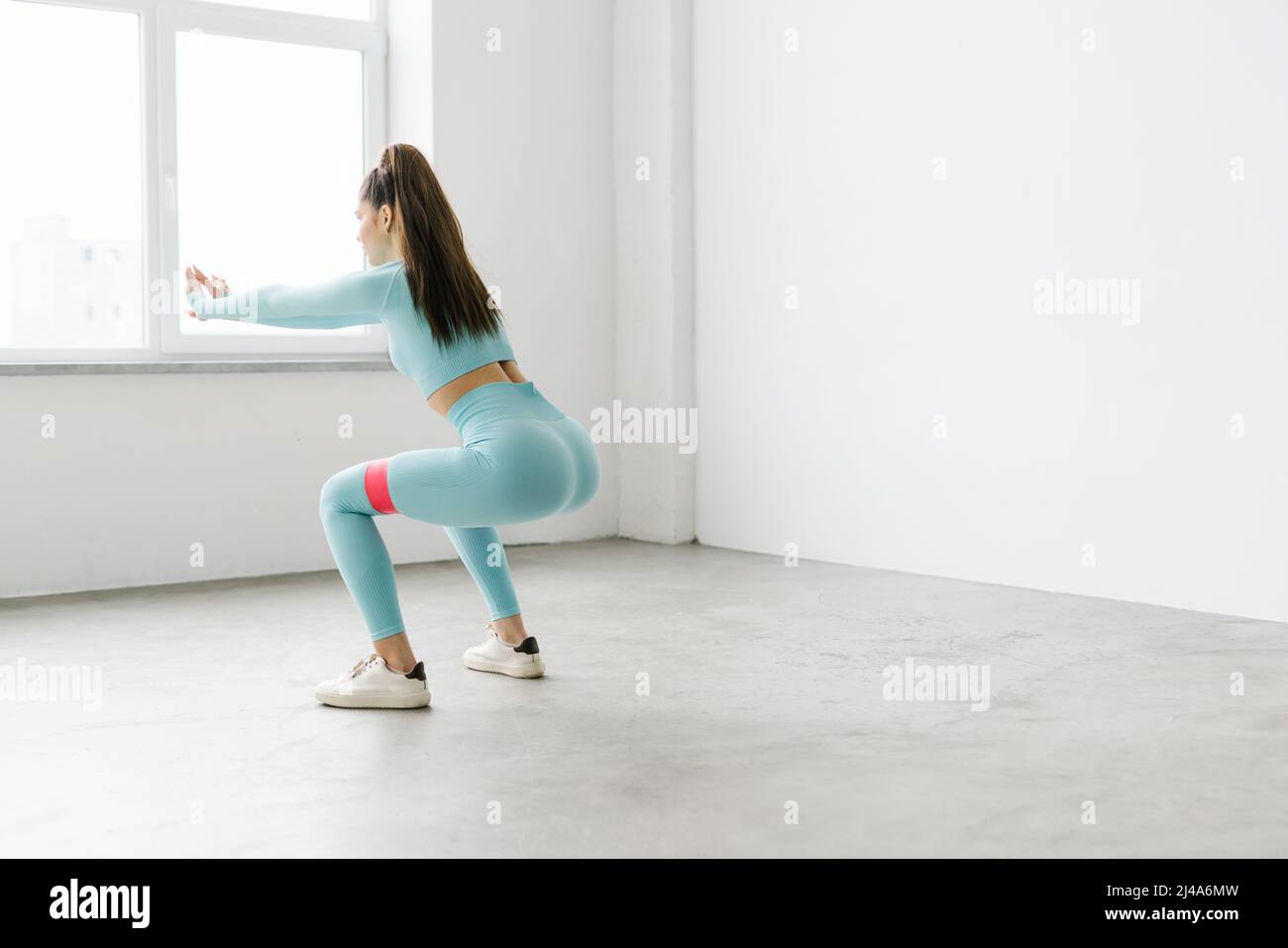 Slim woman works out with resistance band on white wall background ...