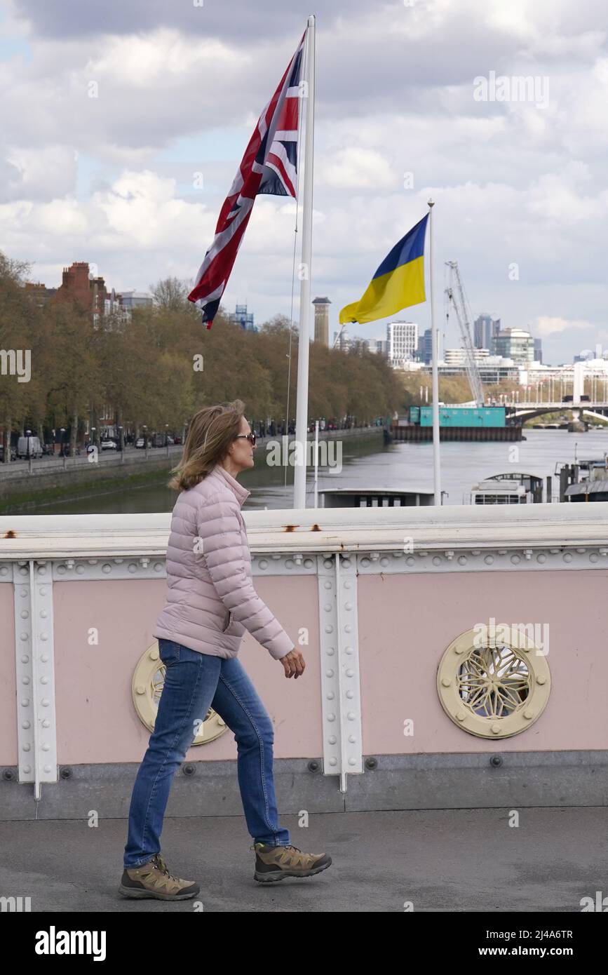 A woman walks across Albert Bridge as a Ukrainian flag (right) is ...
