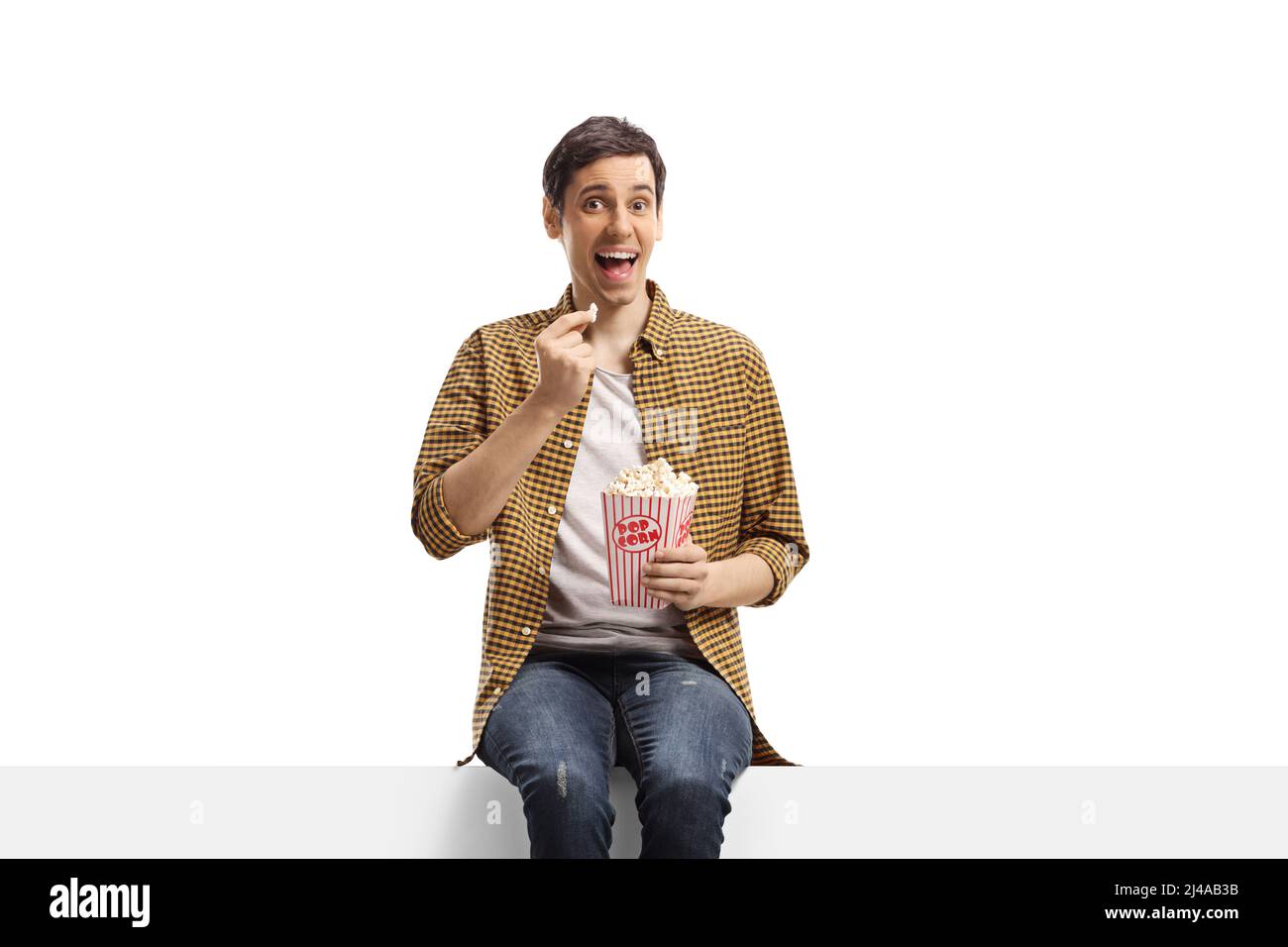 Excited young man sitting on a panel and eating popcorn isolated on ...
