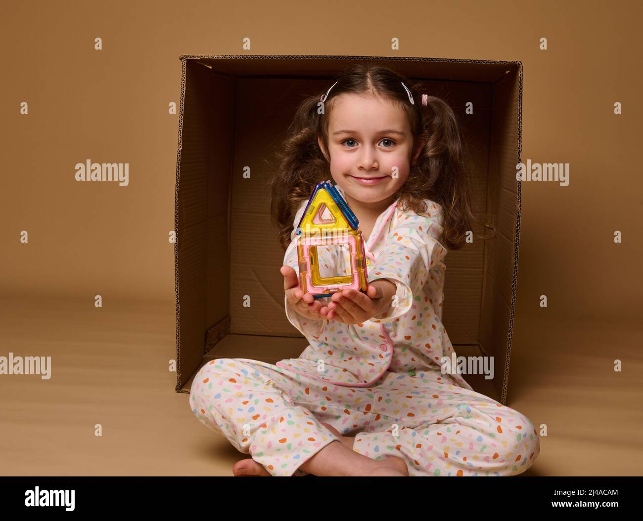 Little Caucasian girl in pajamas holding a colorful house built from ...