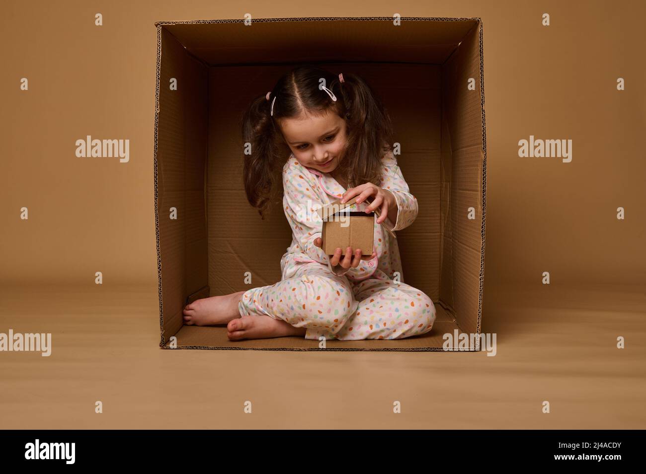 Adorable Caucasian child girl hiding inside a box and playing with a ...