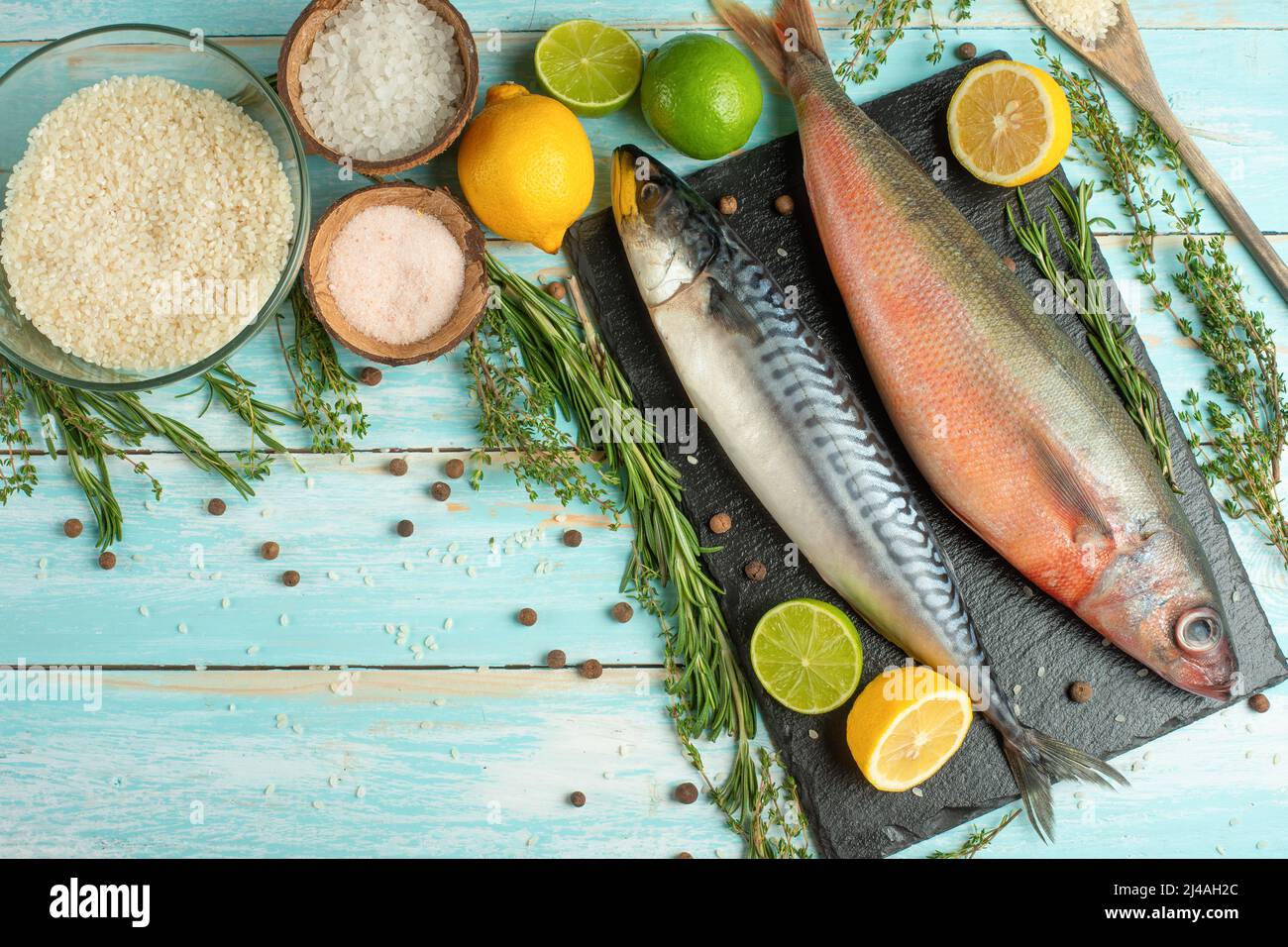Two fresh fish on a black slate stone with spices, herbs, lemon, lime ...