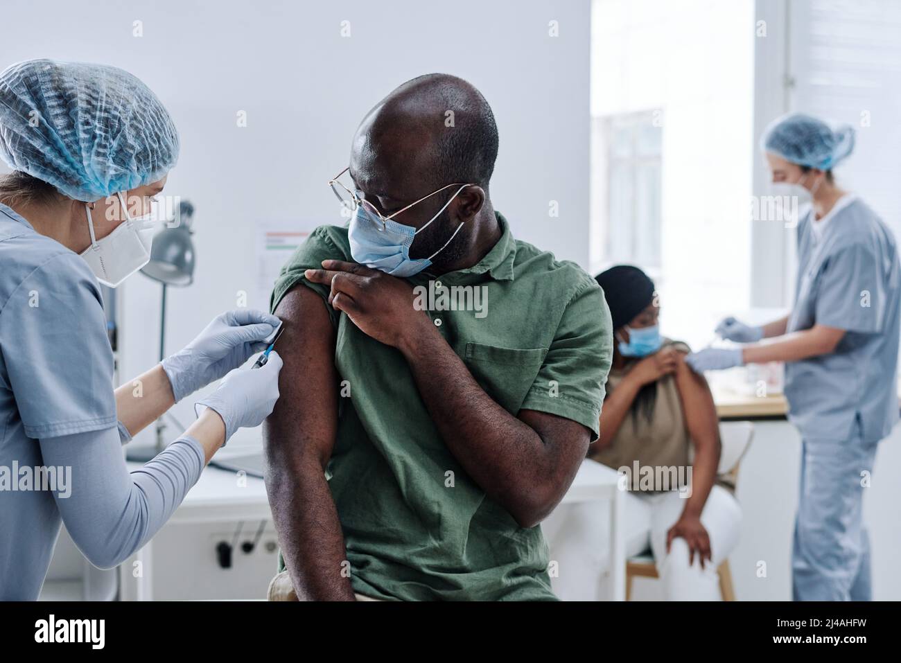 African guy in mask preparing his shoulder while doctor giving an ...