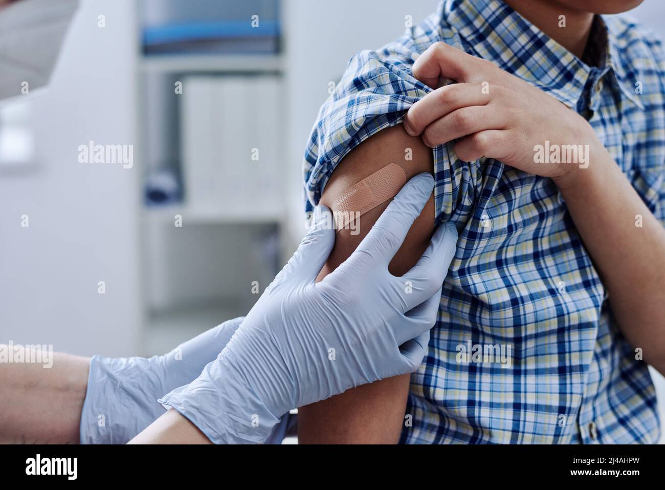 Close-up of nurse applying plaster on shoulder of little boy during ...