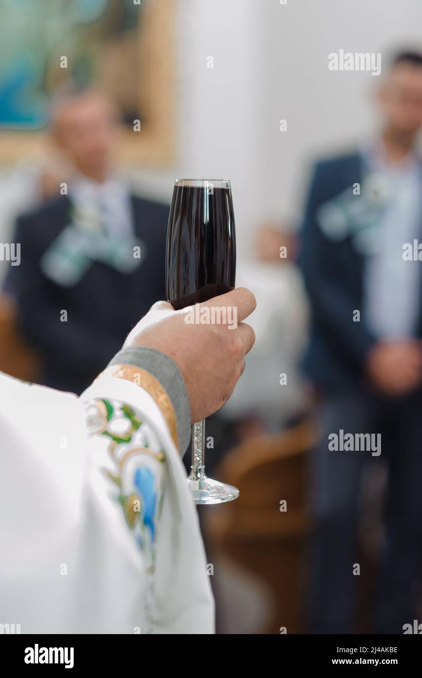 The priest holds a glass of red wine in his hand. Church religious ...