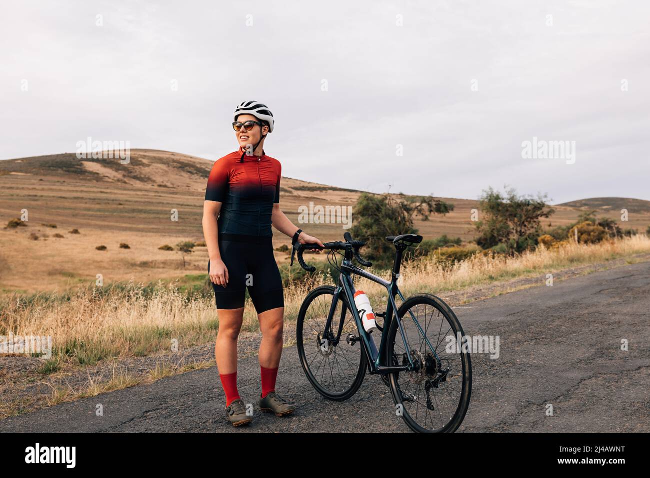 Female cyclist taking break from riding bike standing on empty road ...