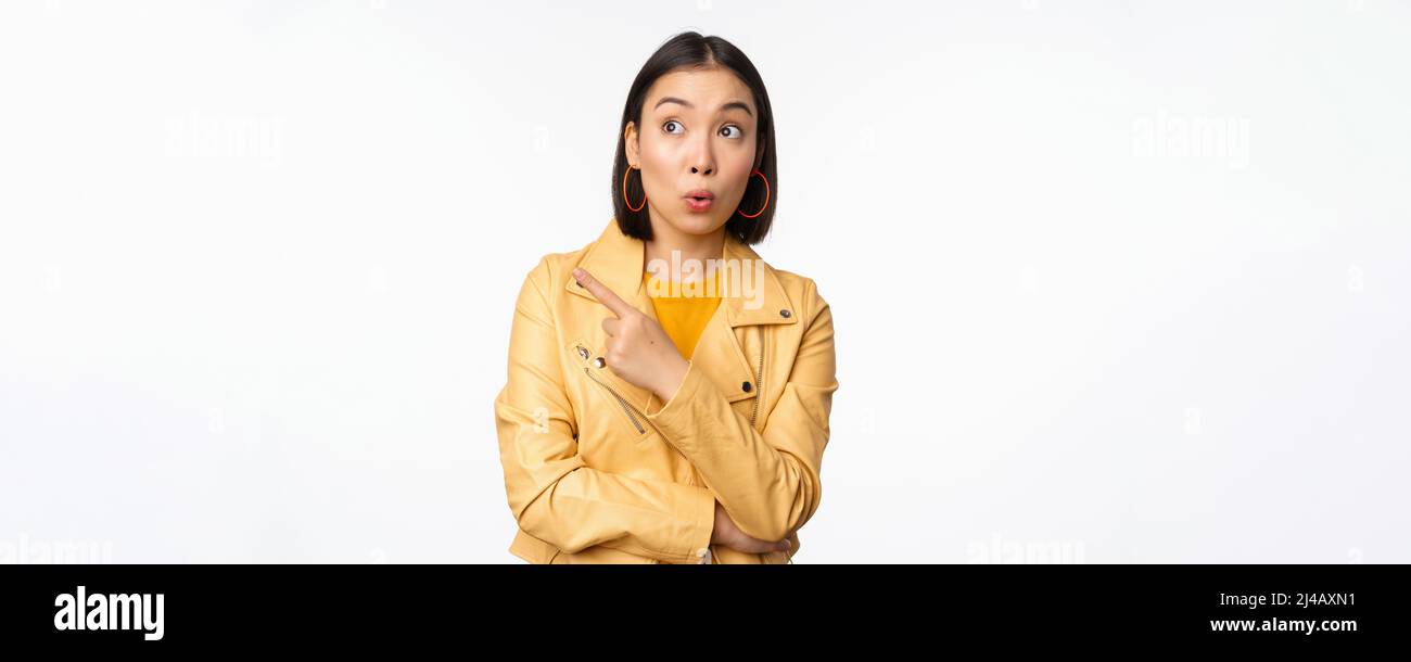 Image of surprised aisan woman pointing finger left, looking at logo or ...