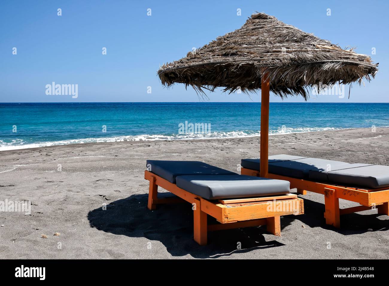 Sun beds and a sun umbrella at the famous black sandy beach of Perissa ...