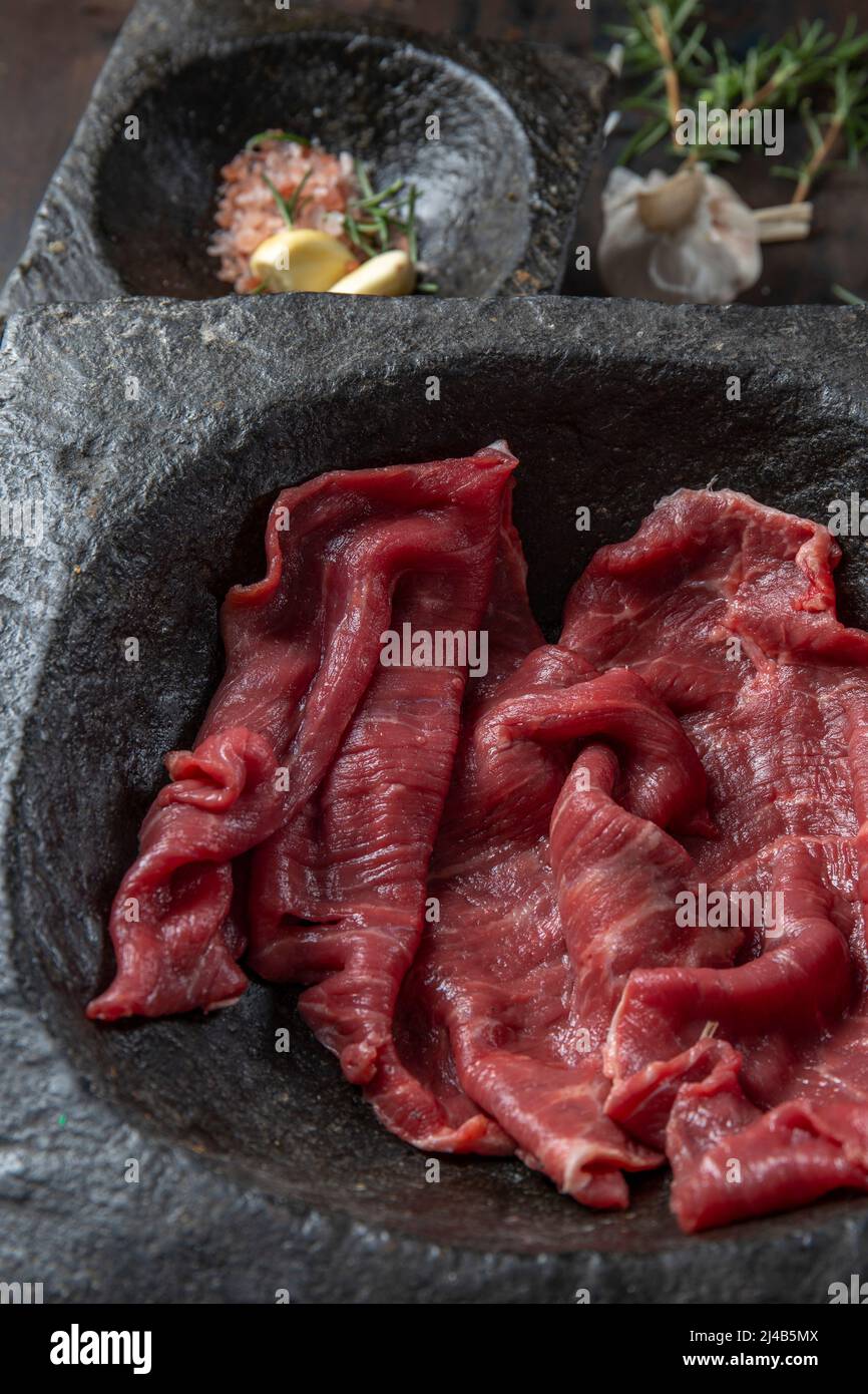 Raw beef fillet on black stone plate and mortar with herbs. Black ...