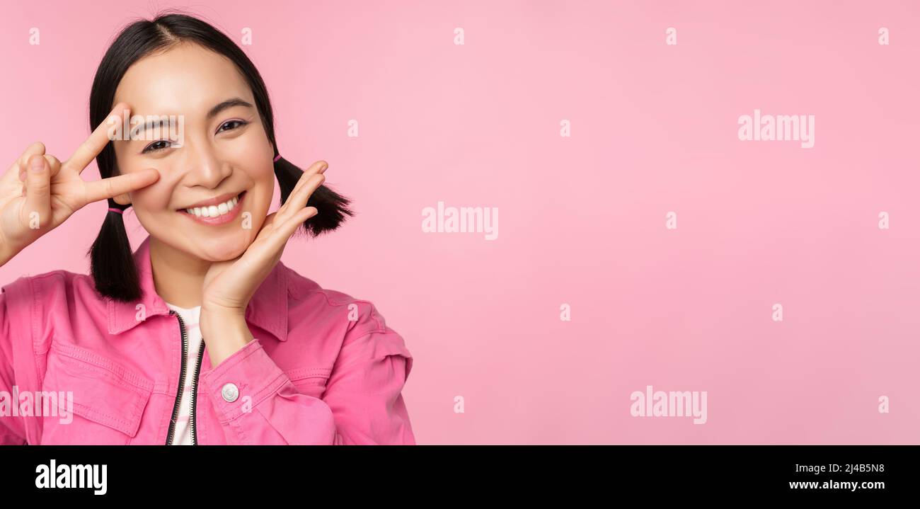 Close up of stylish asian girl smiles happy, shows peace v-sign, kawaii ...