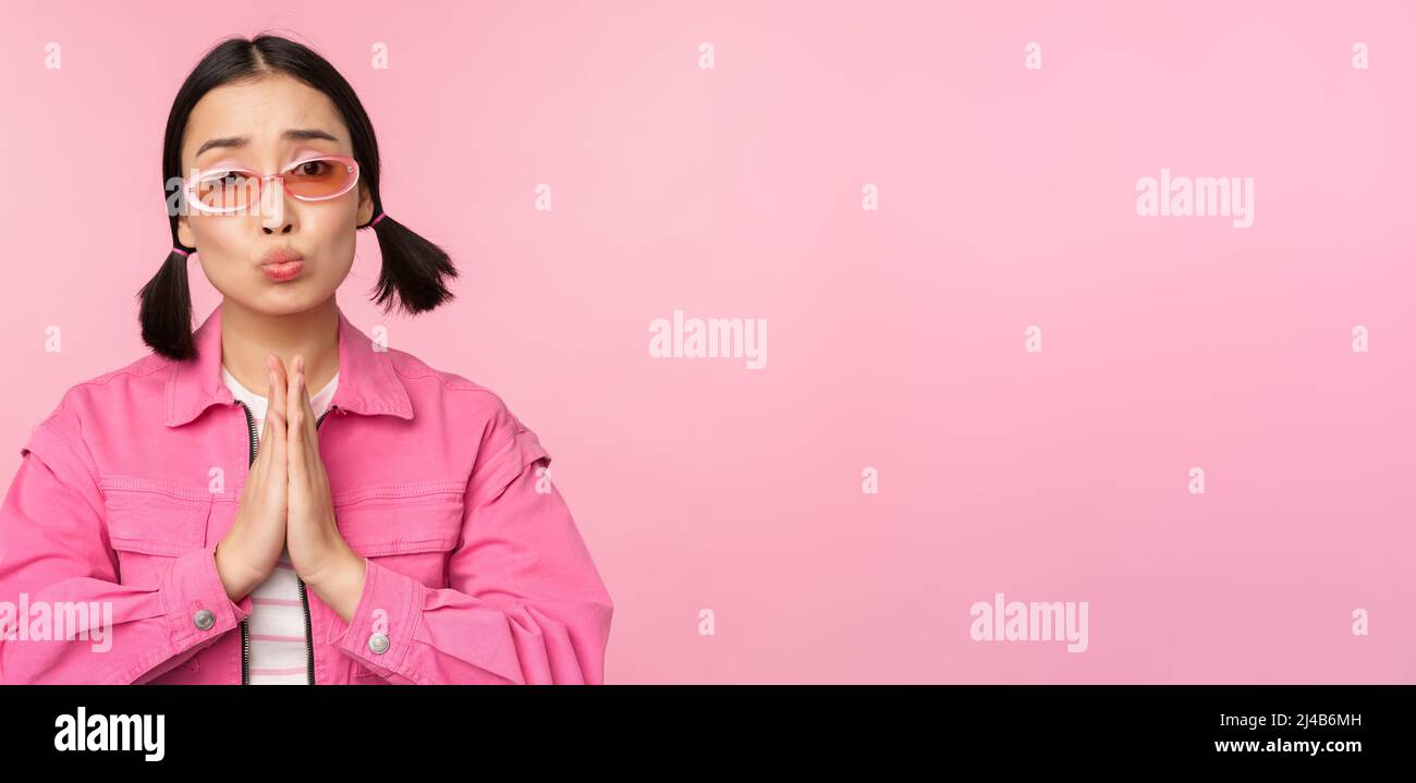 Please. Cute asian girl asking favour, begging, standing against studio ...
