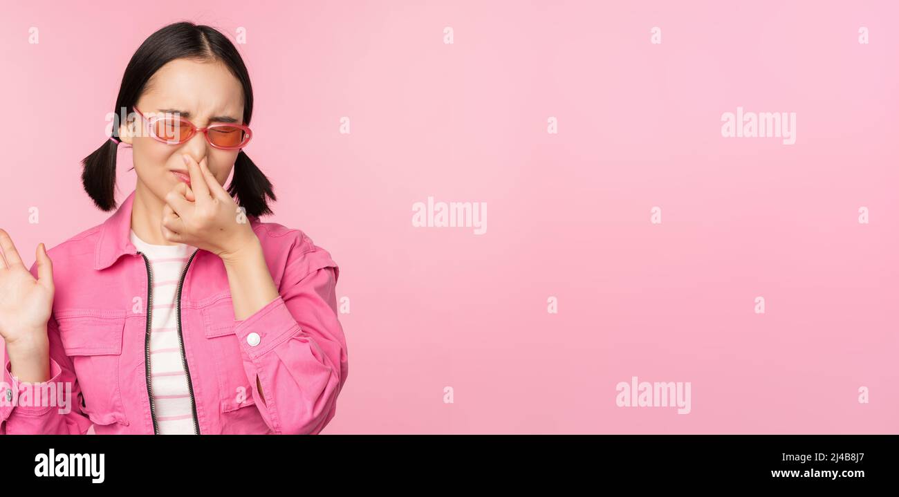 Stinky. Asian girl in sunglasses and stylish outfit, shuts her nose ...