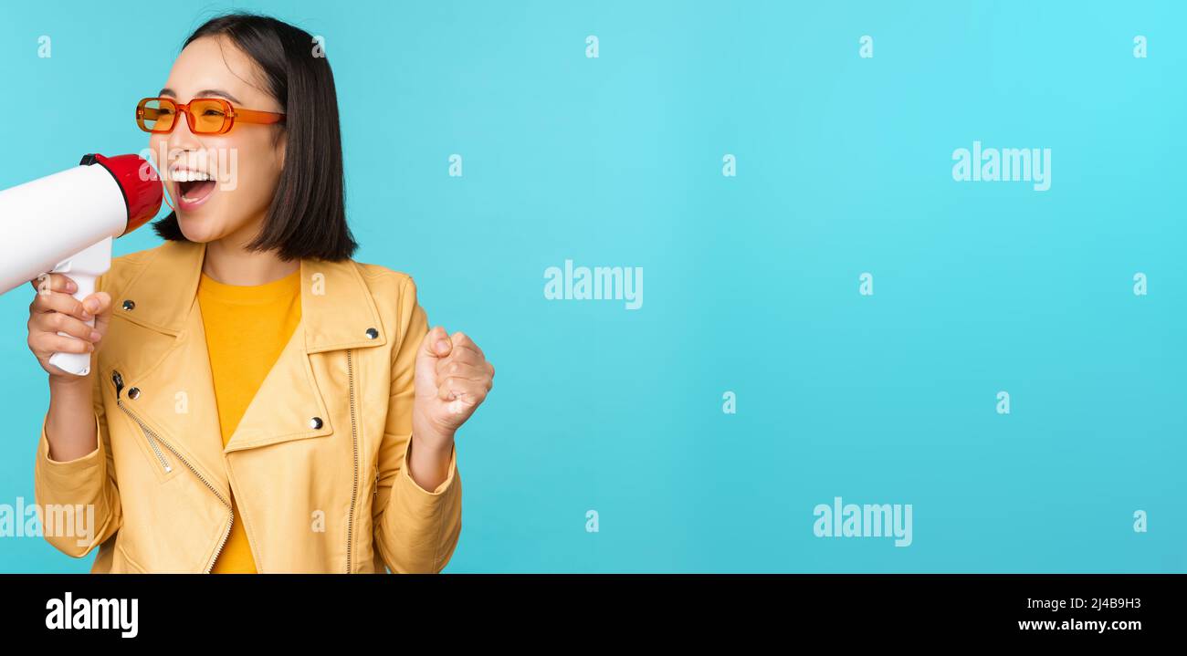 Young enthusiastic korean girl in trendy outfit, shouting in megaphone ...