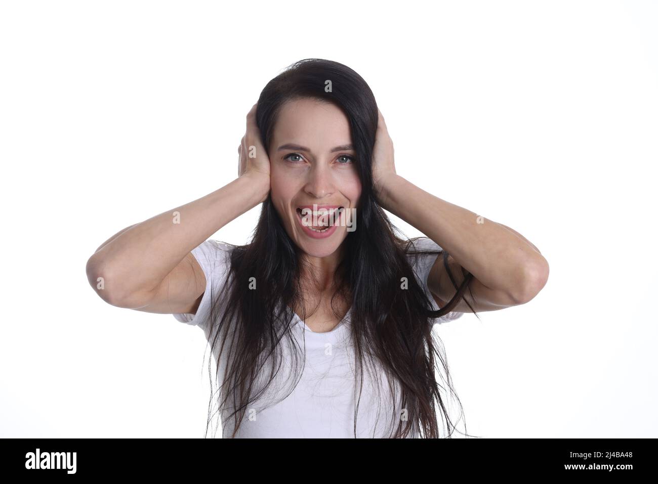 Young brunette woman covering ears with hands, open eyes, screaming ...