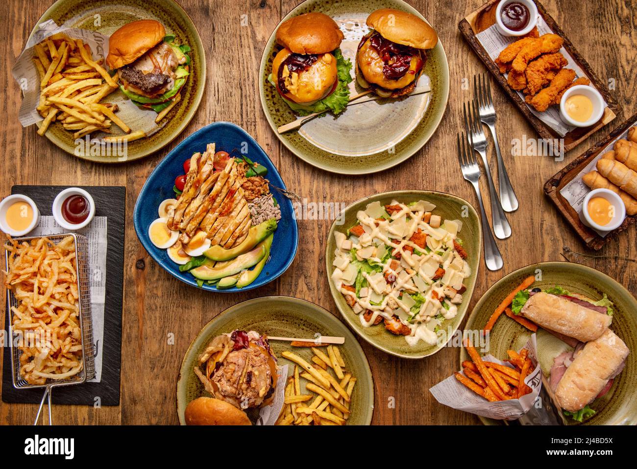 Set of fast food dishes on wooden table with assorted burgers ...