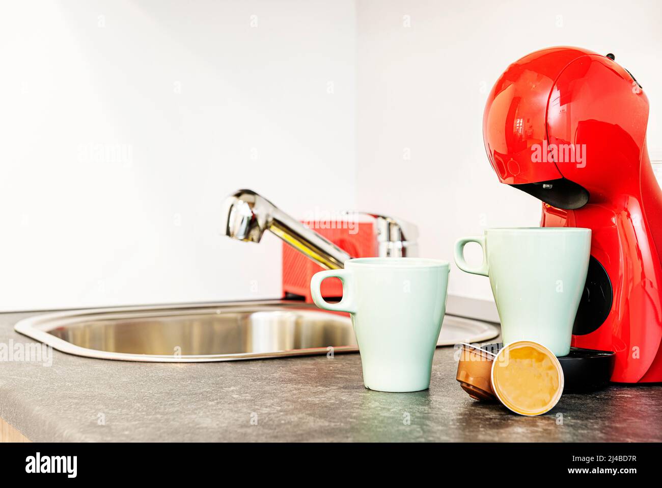 Red capsule coffee maker and light green cups on a dark gray countertop ...