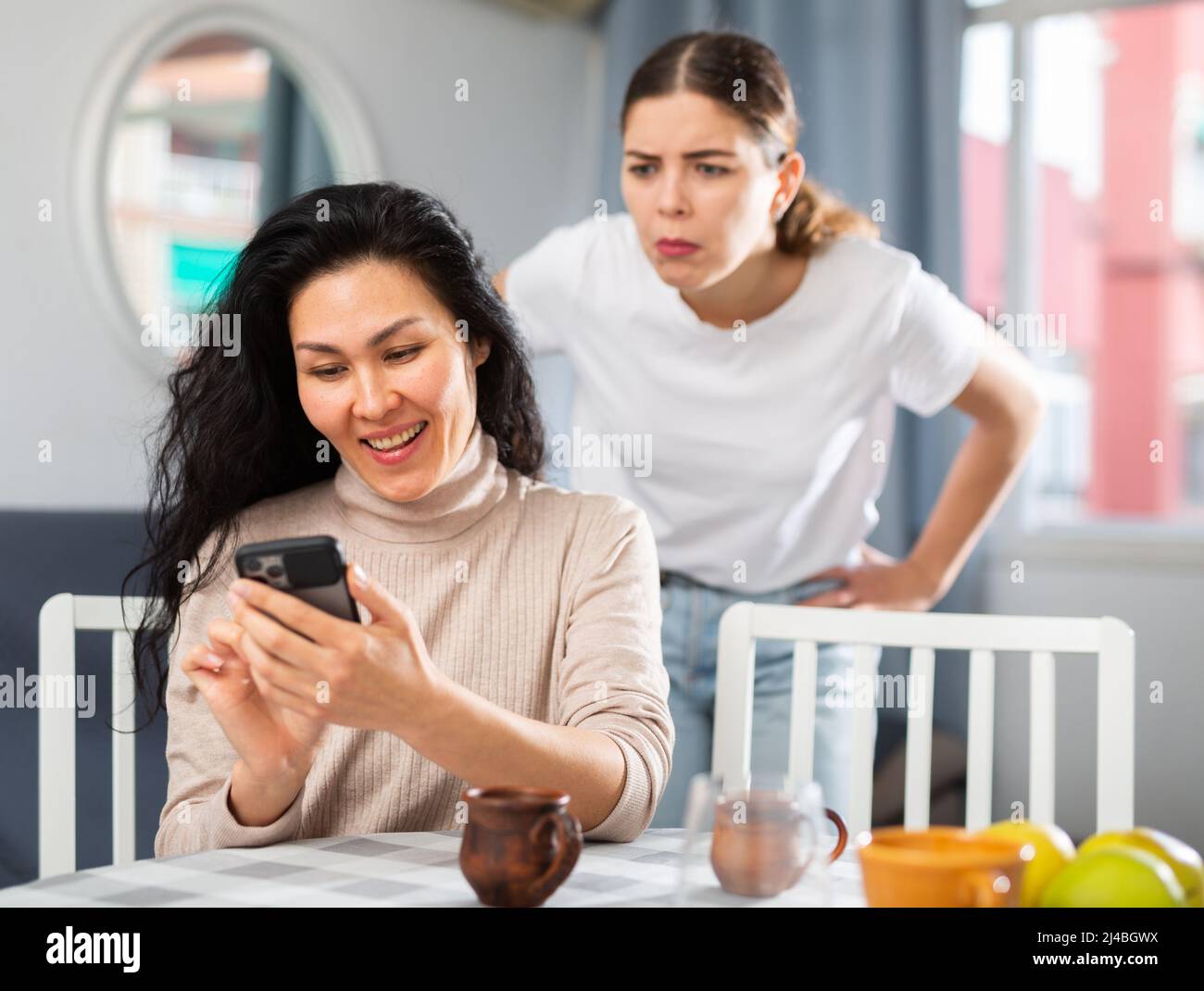 Friend peeks over her shoulder as a woman types a text message on phone ...