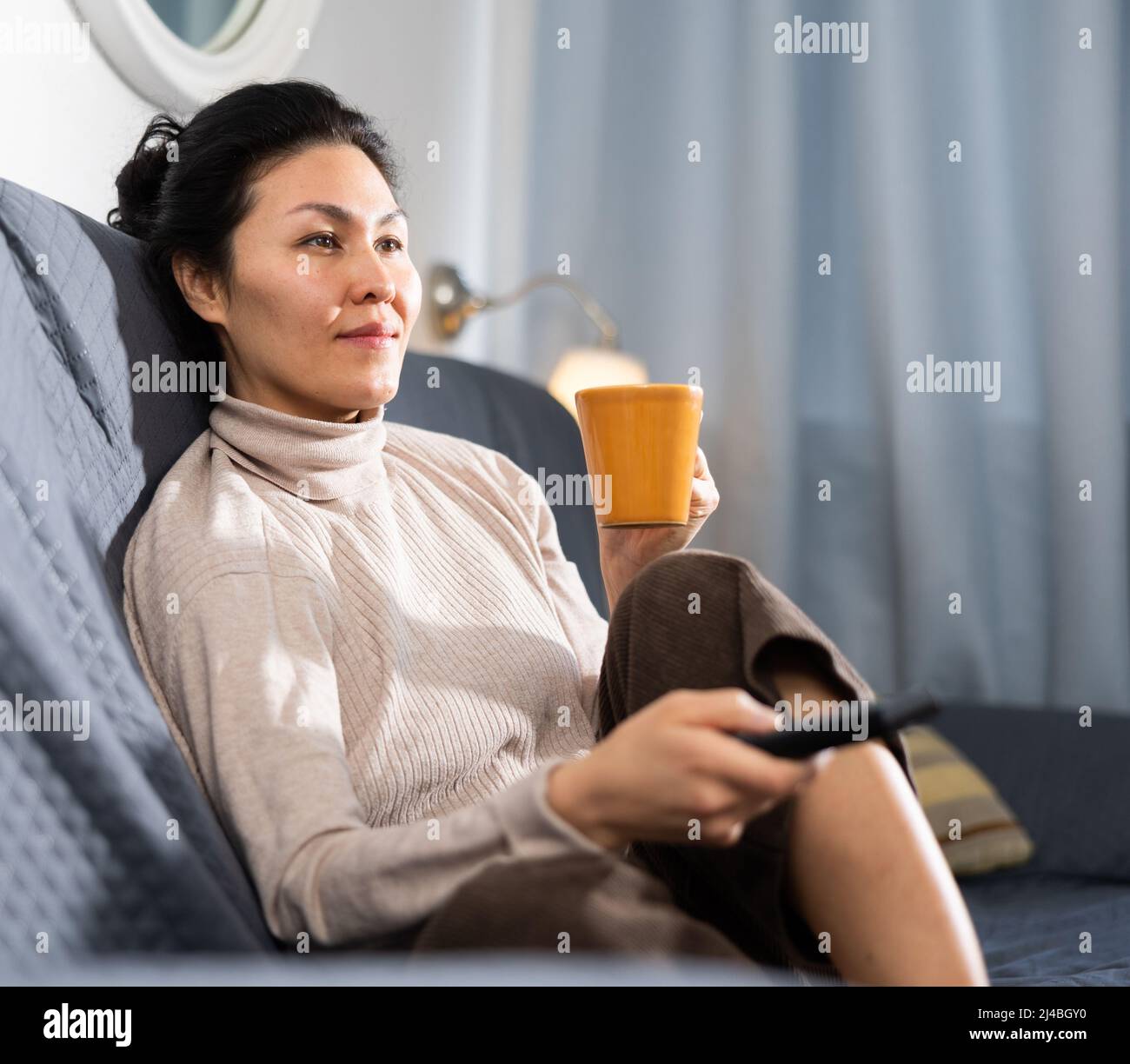 Asian woman watching TV at home Stock Photo - Alamy