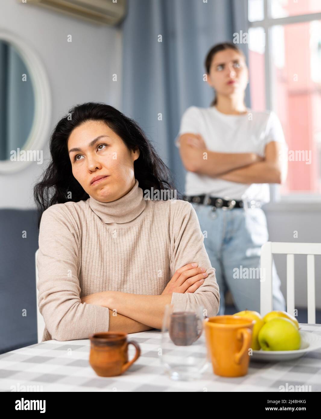 Upset woman sitting at home table with disgruntled woman behind Stock ...
