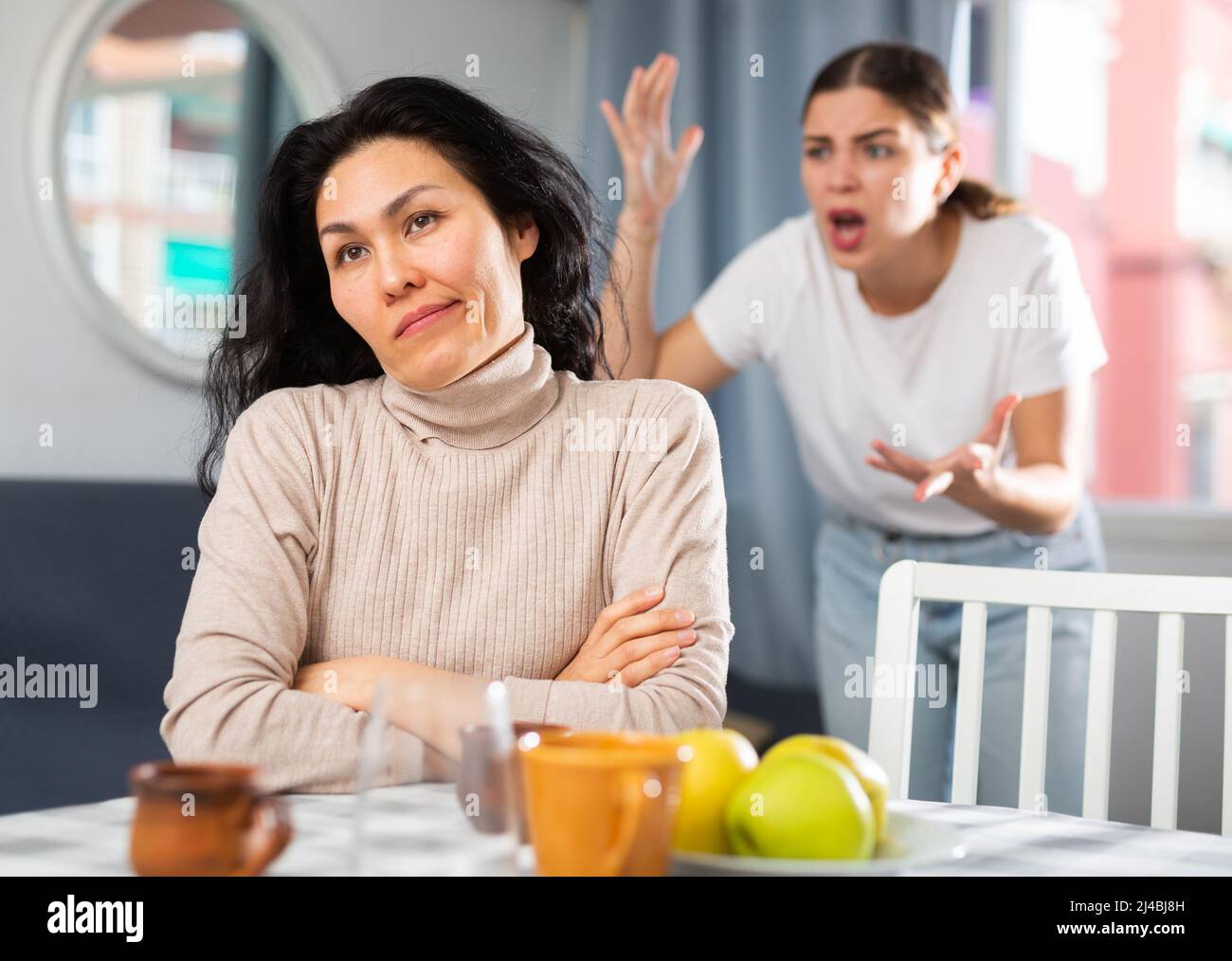 Upset woman sitting at home table with disgruntled woman behind Stock ...