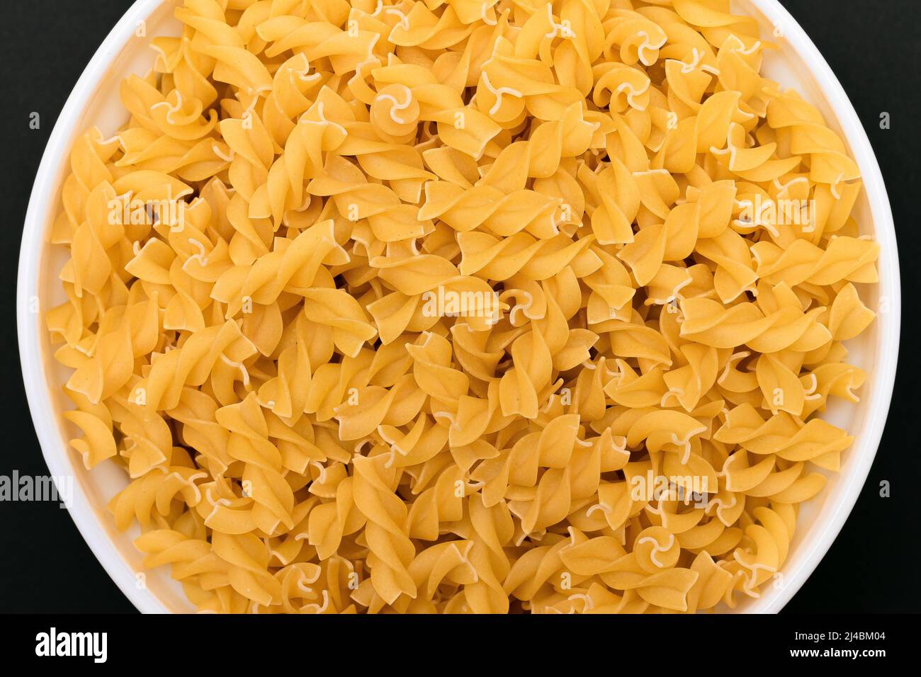 Uncooked Fusilli Pasta Lying on White Plate on Black Background. Raw ...