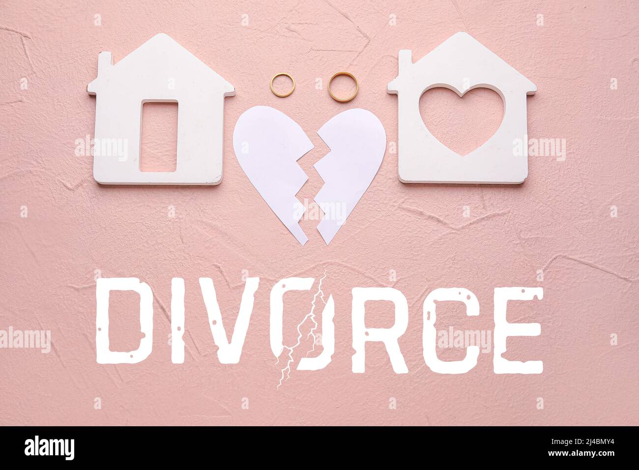 Figures of houses, broken paper heart and wedding rings on pink ...