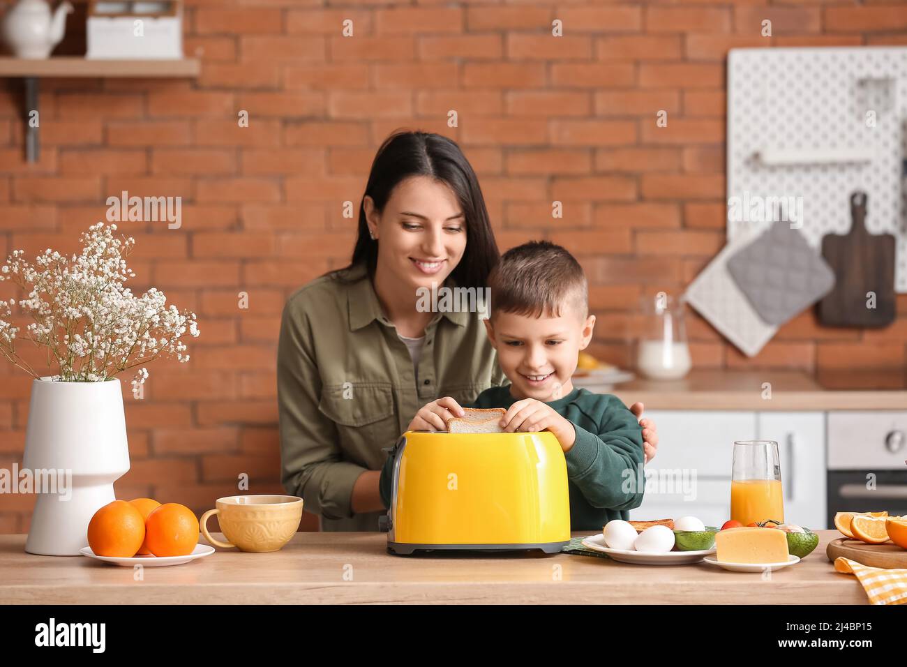 Little boy with his mother putting bread slices into toaster in kitchen ...