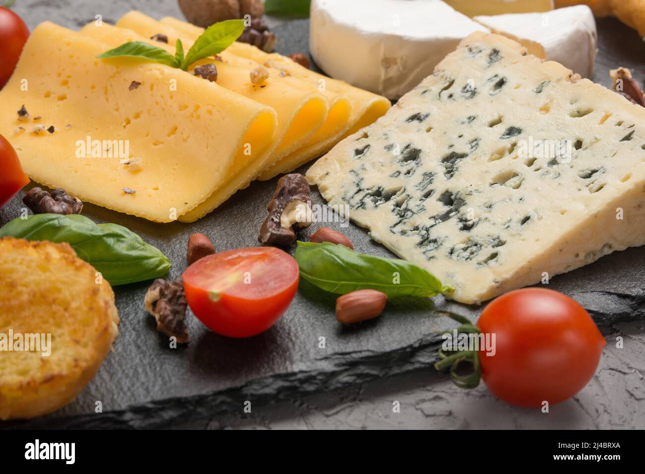 Different kinds of cheeses on a black board, with cherry tomatoes and ...