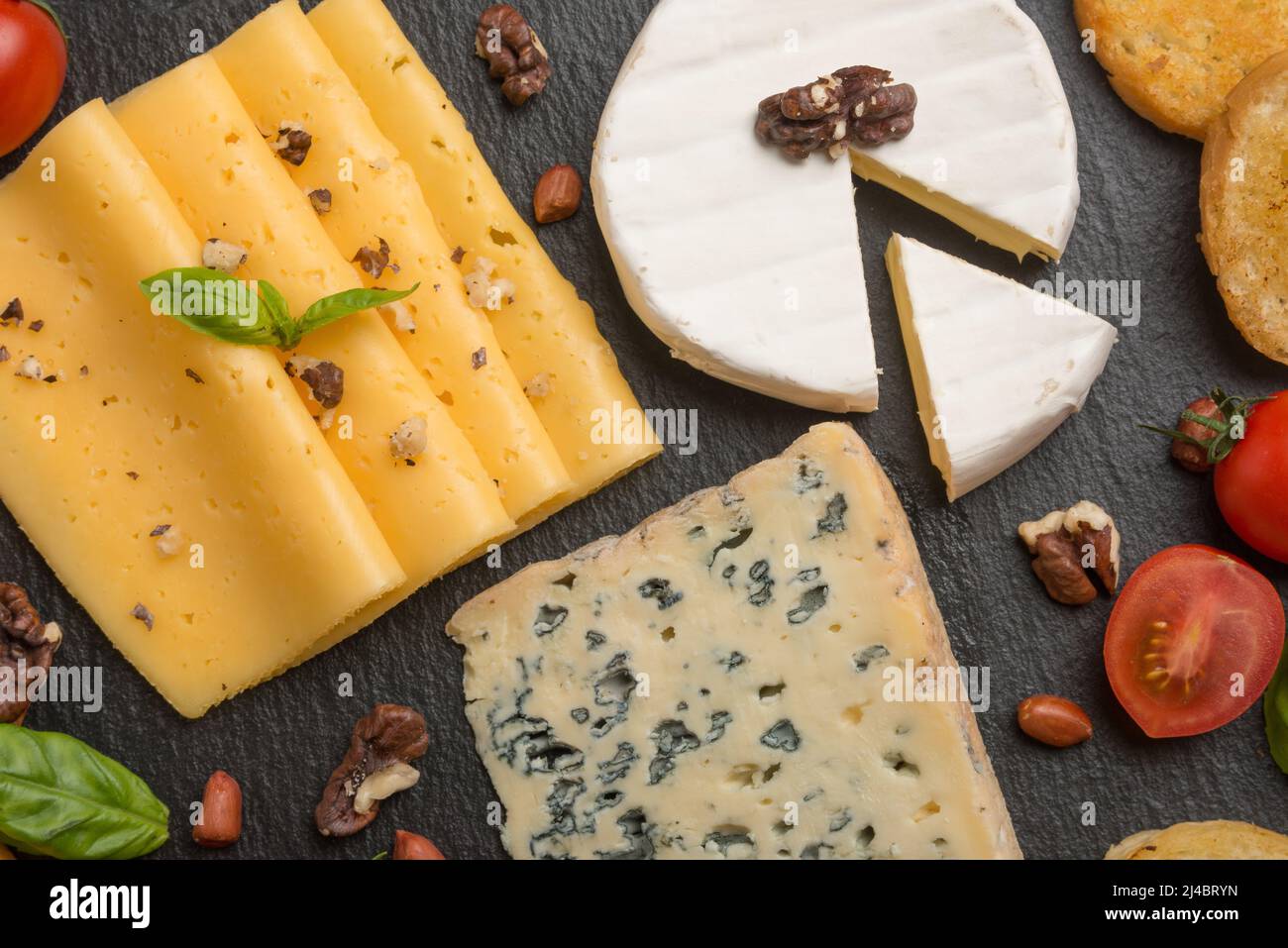 Different kinds of cheeses on a black board, with cherry tomatoes and ...