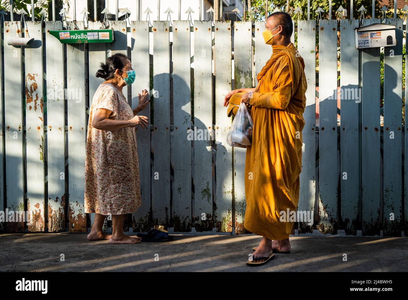 A woman gives alms to a monk outside of her home at sunrise in Bangkok ...