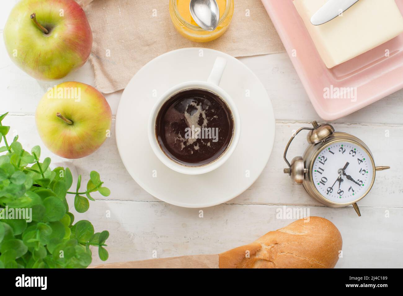Morning cup of coffee, alarm clock, apples, butter and baguette, in a ...