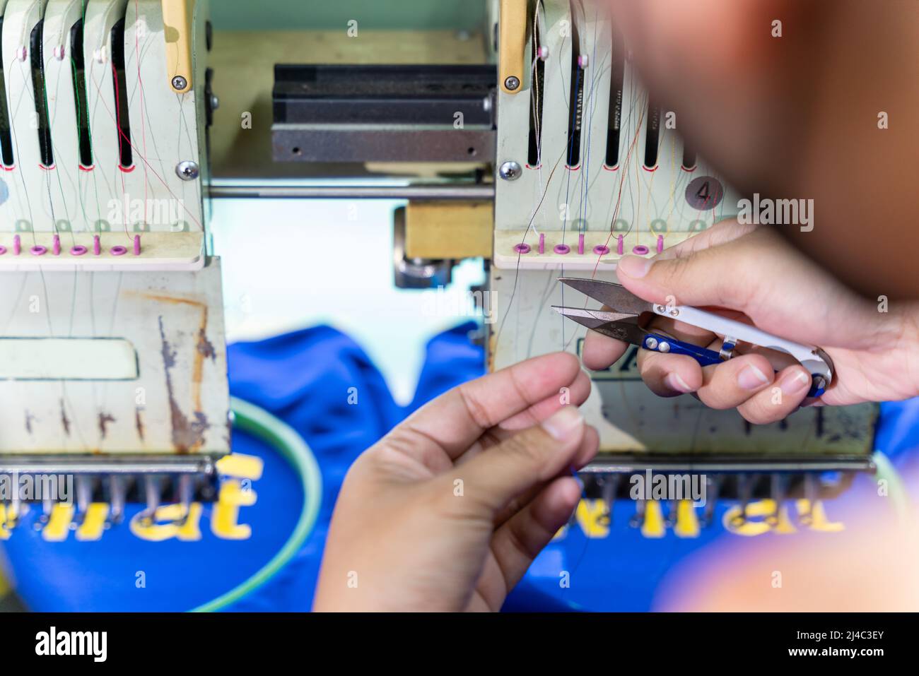 A worker use scissors to cut yarn on sewing machine. Embroidery area in ...