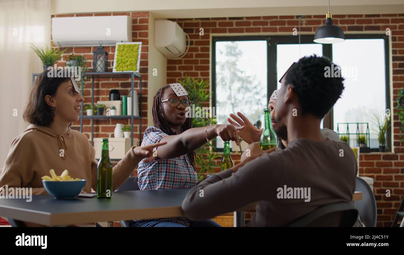 Cheerful people guessing cards on forehead at fun gathering, enjoying ...
